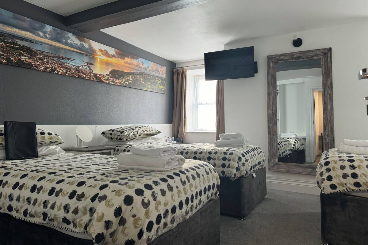 Quarto de hotel com duas camas, uma pintura grande, uma TV de tela plana e uma janela com cortinas.