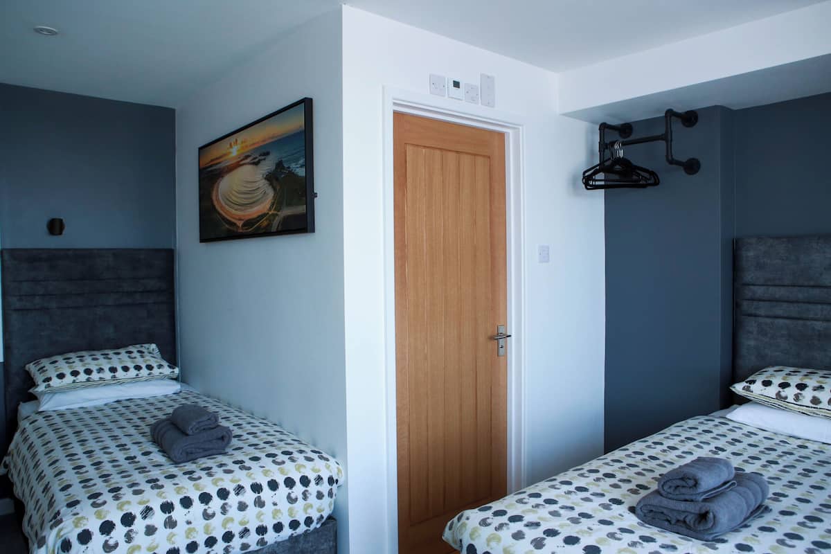 Quarto com duas camas, porta de madeira, um quadro e um cabide fixado na parede.