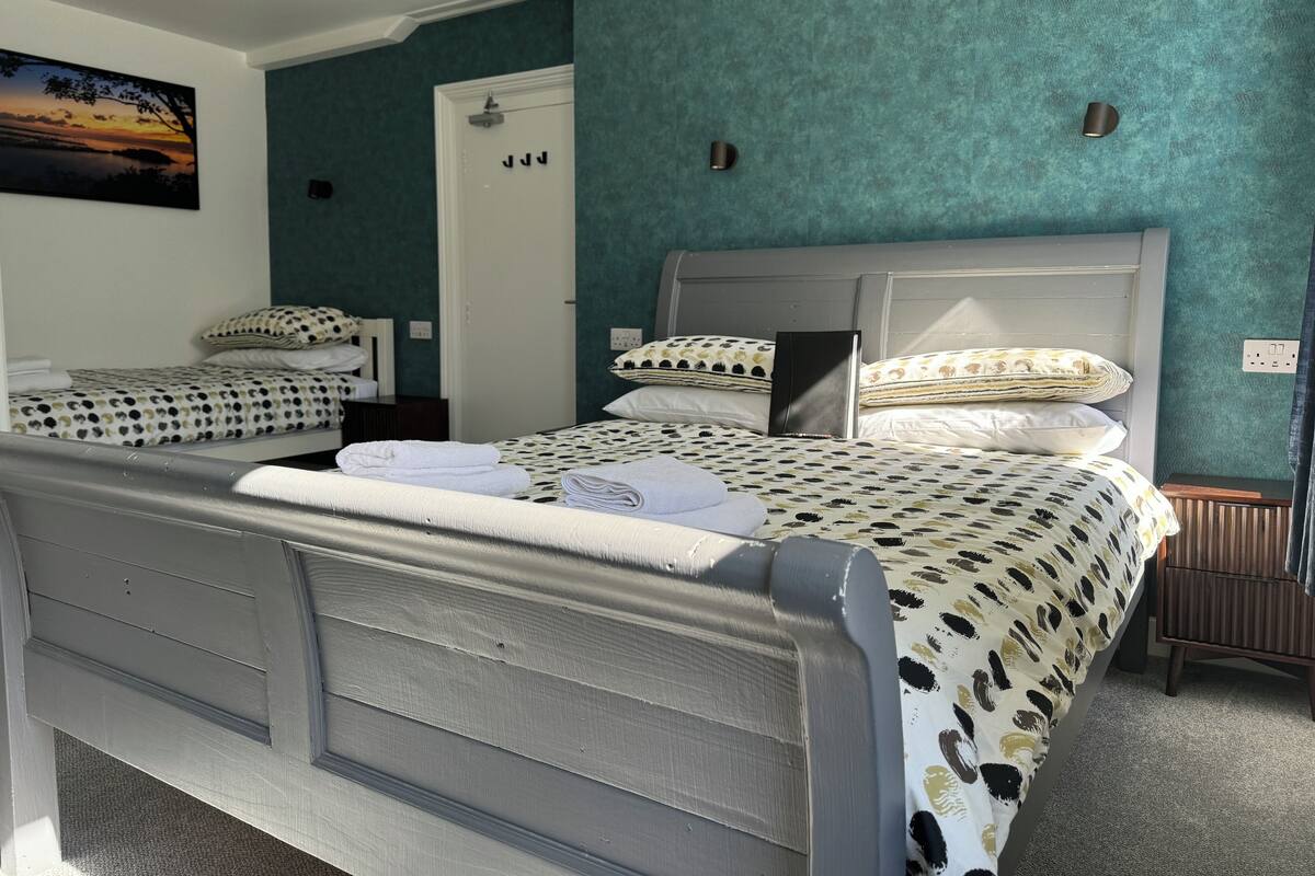 Quarto de hotel com duas camas de solteiro, banheiro e parede cor de verde-água.