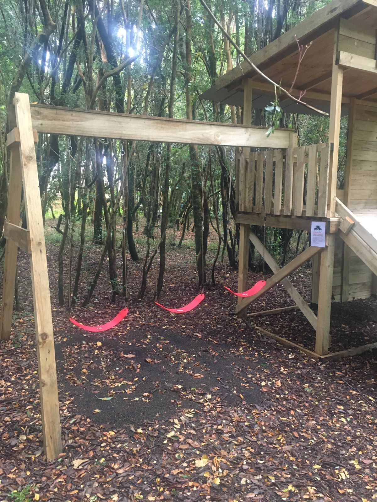 Um conjunto de baloiço de madeira com bancos vermelhos numa área arborizada.
