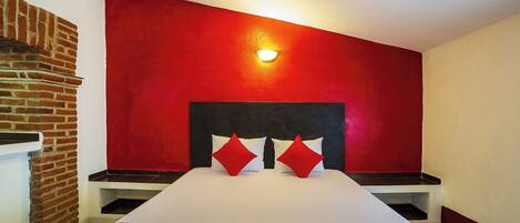 Quarto de hotel com parede de tijolos, parede de destaque vermelha, cabeceira preta, colcha branca e duas almofadas vermelhas.
