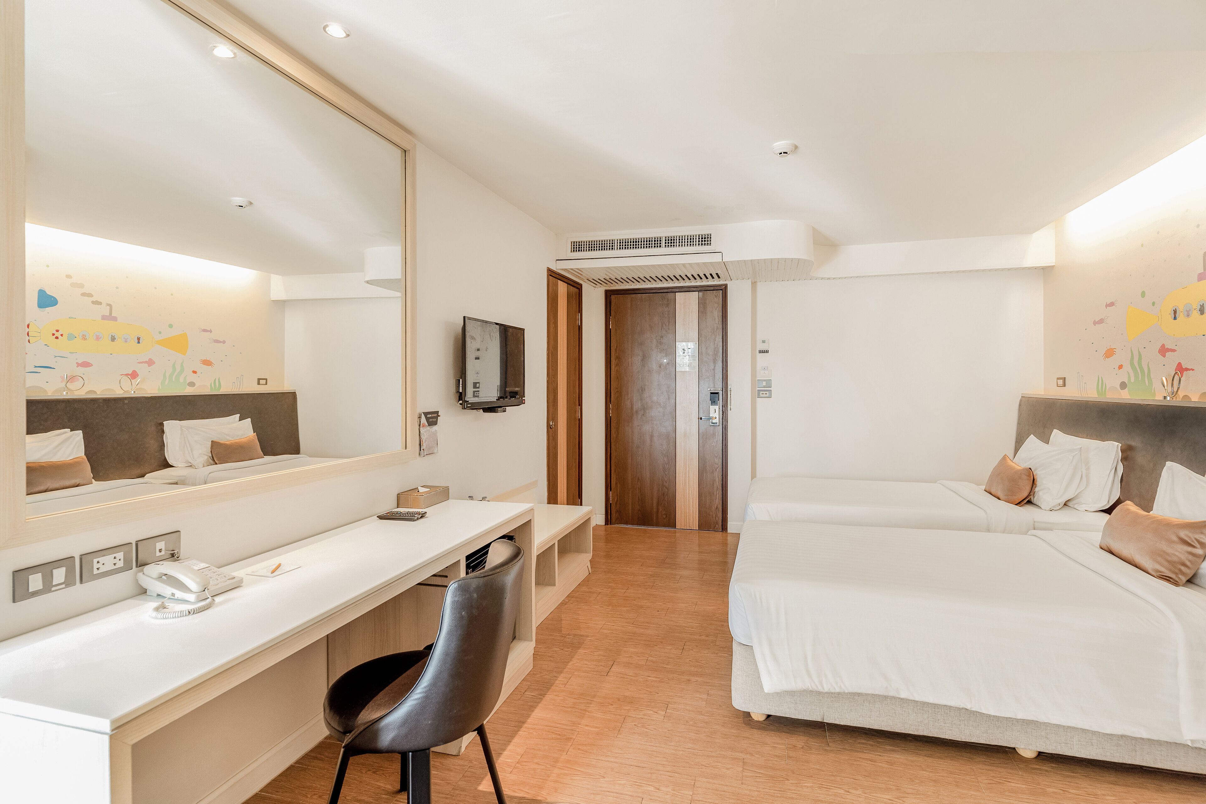 Quarto de hotel com cama, escrivaninha, cadeira, espelho e porta para o banheiro.