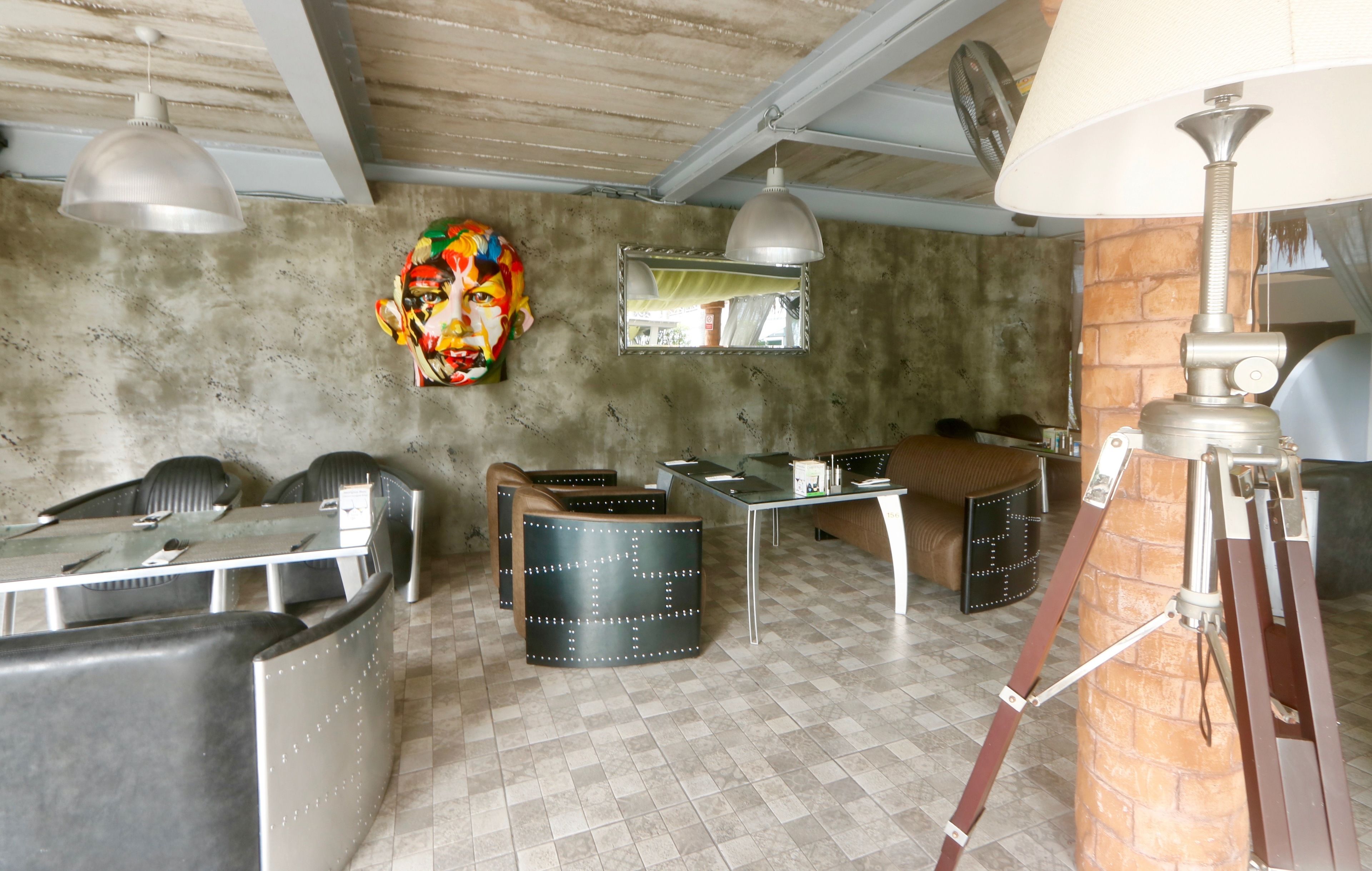 Um restaurante com assentos em cabines, uma grande máscara decorativa na parede e piso xadrez.