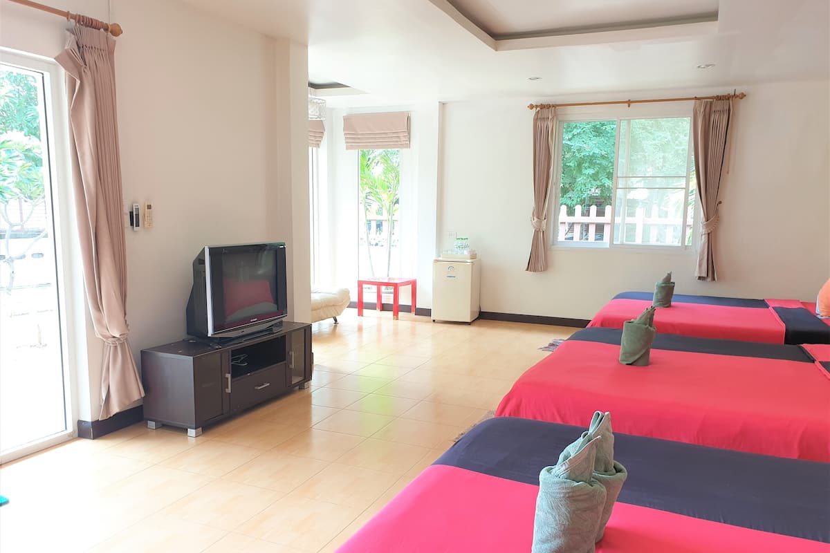 Quarto de hotel com televisão em suporte, mini-frigorífico, uma cadeira vermelha e duas camas com roupa de cama vermelha e azul.