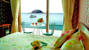 Quarto com cama, mesa com frutas e vista para o mar e uma ilha.