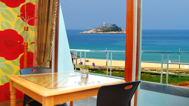 Quarto com vista para o mar, uma mesa, cadeiras e uma janela com cortinas.