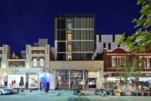 Um edifício moderno com fachada de vidro e base de tijolos, cercado por outros edifícios comerciais.