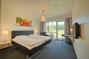 Quarto de hotel com uma cama grande, uma escrivaninha, uma cadeira, uma televisão e um quadro na parede.