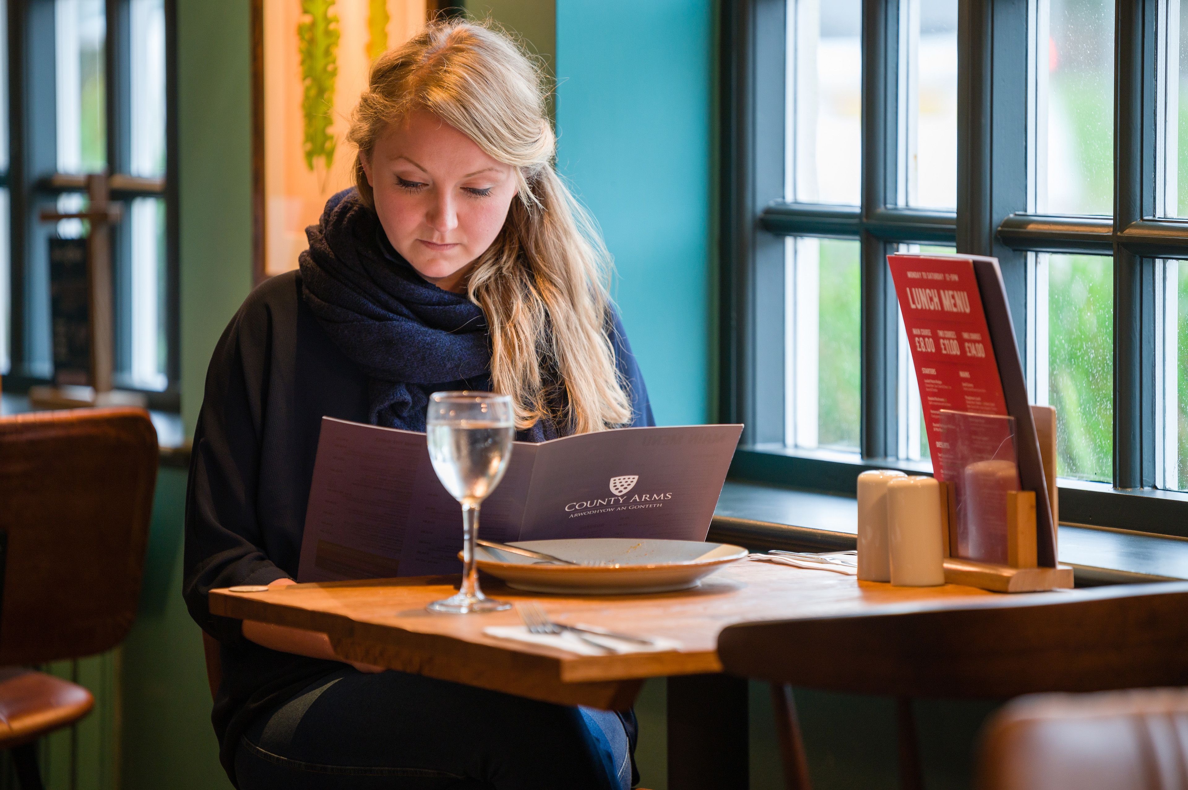 Uma pessoa sentada à mesa com um laptop, um menu e um copo de água.