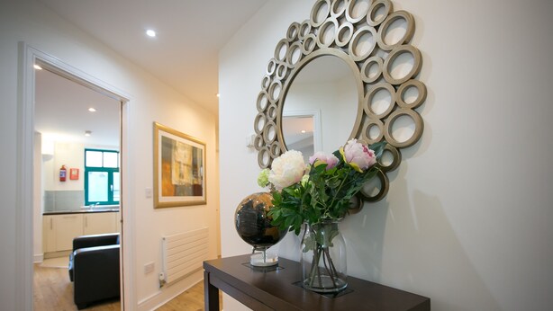 Um corredor com um espelho decorativo de moldura circular, um console de madeira escura e um vaso com flores.