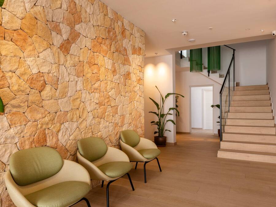 Decoração moderna com parede de pedra, escada e cadeiras verdes.