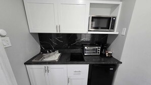 Uma cozinha compacta com armários brancos, bancada preta, micro-ondas, torradeira e máquina de lavar louça.