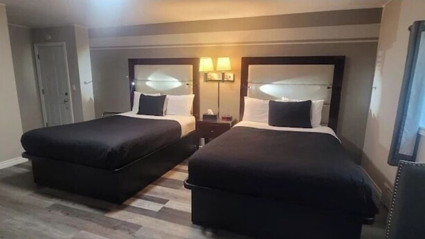 Quarto de hotel com duas camas, uma mesinha de cabeceira, uma luminária e uma janela.