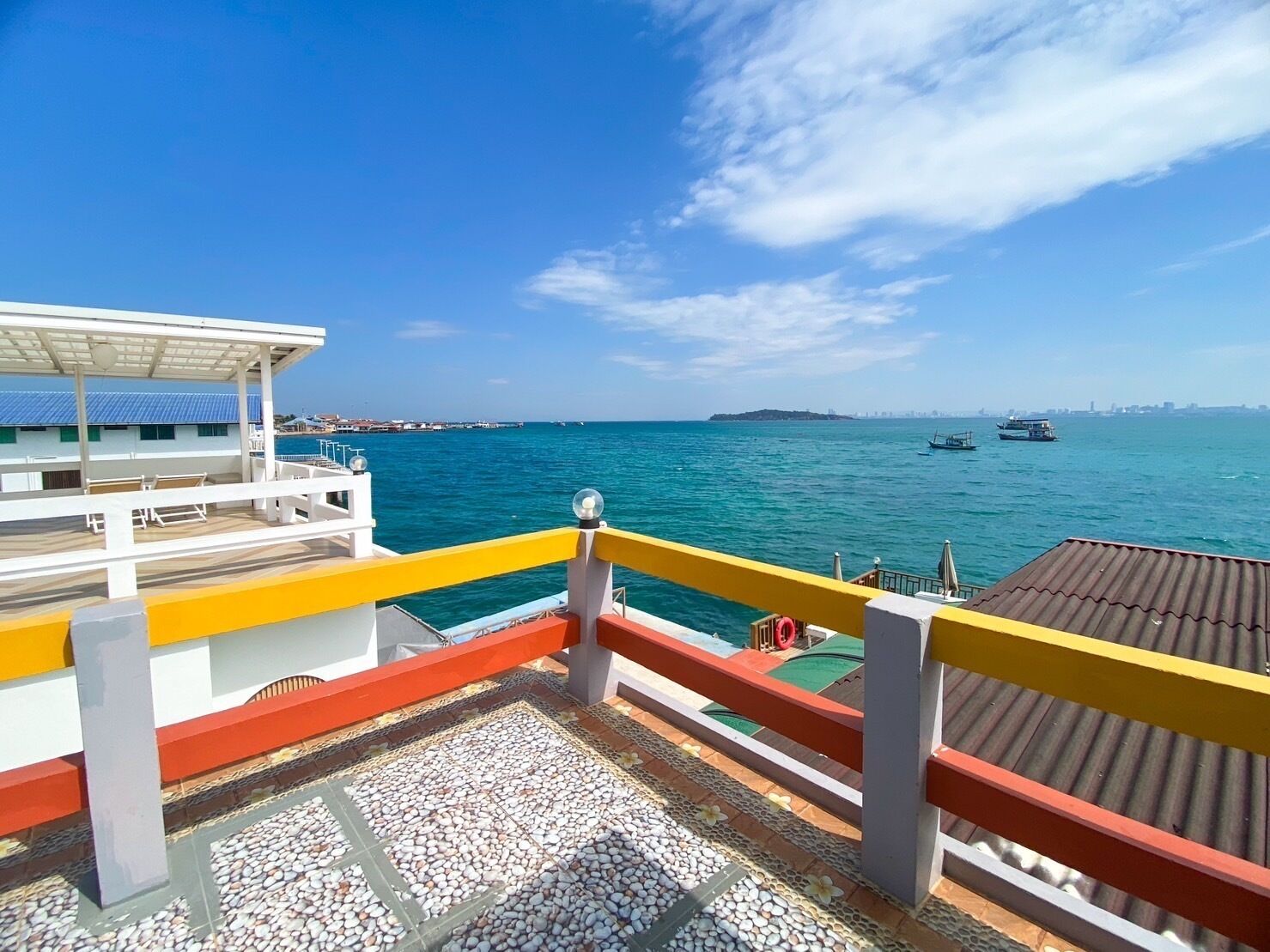 Vista do convés de um barco, com corrimão, piso de pedrinhas e céu azul límpido.