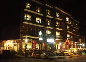 Hotel de vários andares com varandas e uma entrada bem iluminada.
