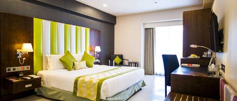 Quarto de hotel com uma cama grande, mesas de cabeceira, escrivaninha e uma televisão.