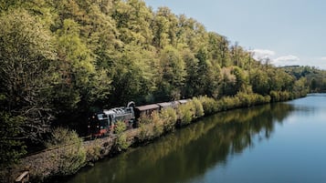 Um trem percorrendo uma margem de rio, cercado por densa floresta.