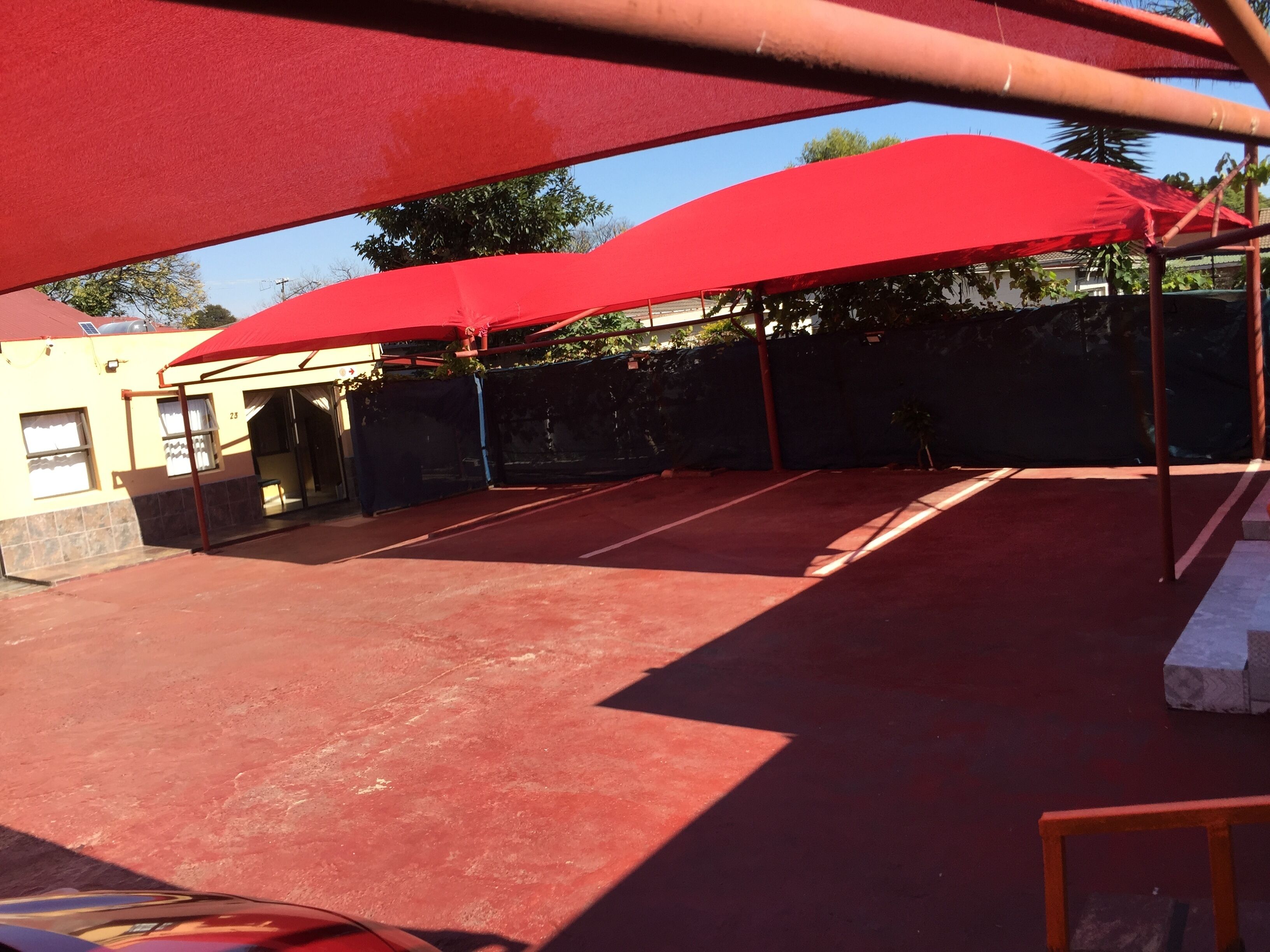 Espaço ao ar livre coberto, com piso vermelho e um edifício ao fundo.