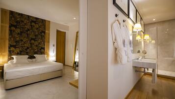Quarto de hotel moderno com uma cama grande, banheiro com pia e espelho, e piso de madeira.