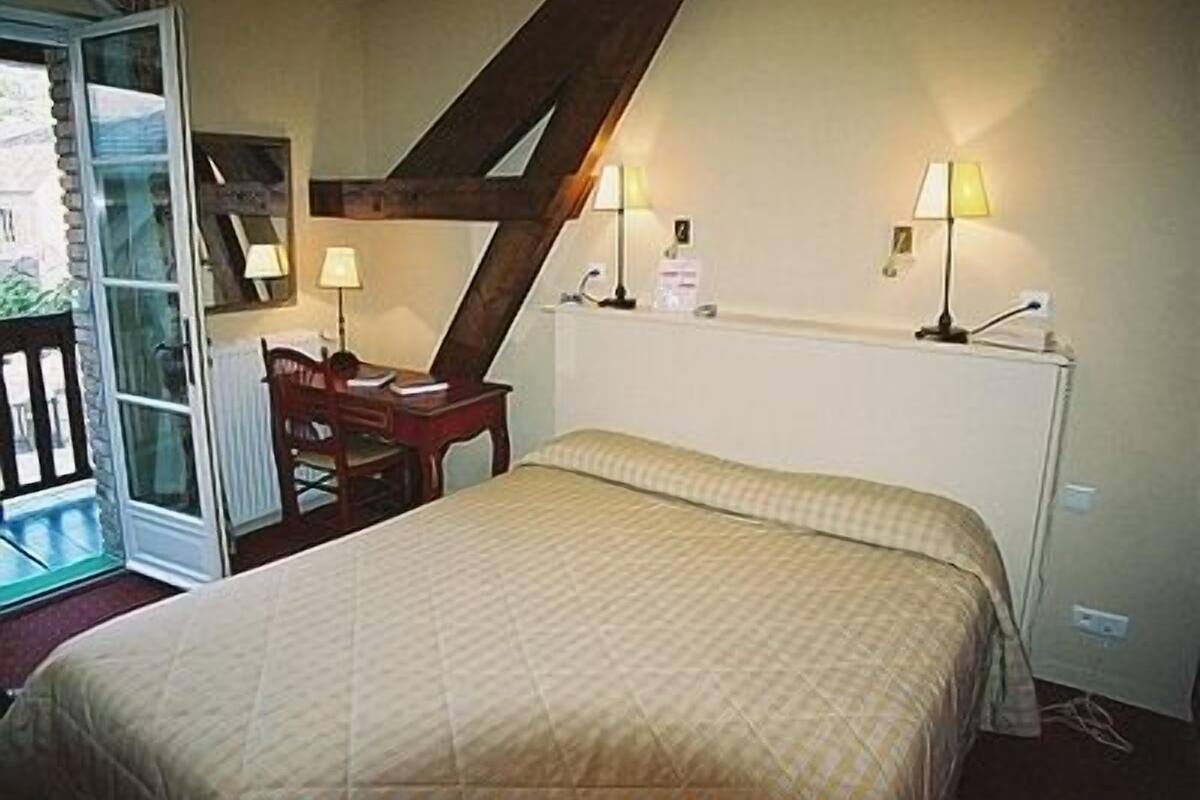 Quarto com cama, escrivaninha, duas luminárias e janela com vista.