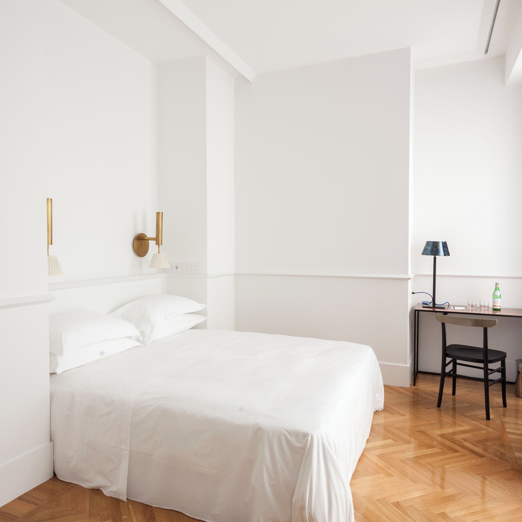 Quarto minimalista com uma cama grande, uma escrivaninha com cadeira e uma luminária.