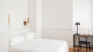 Quarto minimalista com uma cama grande, uma escrivaninha com cadeira e uma luminária.