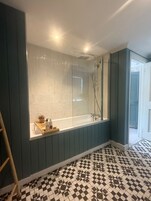 Um banheiro com chuveiro em cabine de vidro, banheira e piso revestido de azulejos.