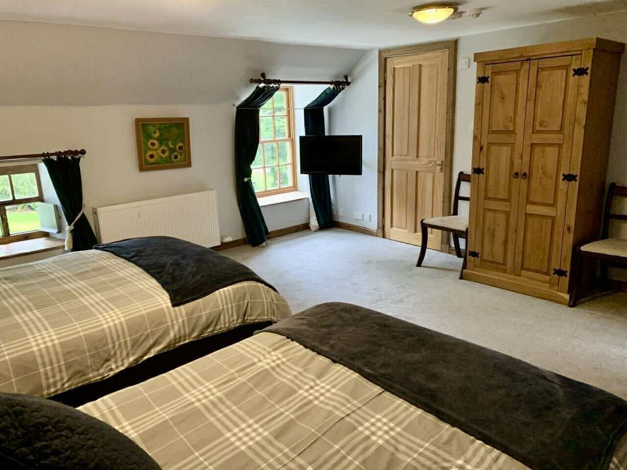 Quarto com duas camas, guarda-roupa de madeira, uma cadeira e janela com cortinas.