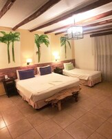 Quarto de hotel com duas camas, um banco de madeira, uma mesa de cabeceira e uma parede com painéis de palmeiras.