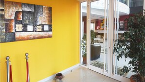 Paredes amarelas vibrantes com uma pintura abstrata moderna, uma porta de vidro que dá para uma varanda com vista, e um vaso de planta.