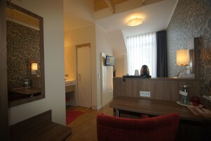Quarto de hotel com uma escrivaninha de madeira, uma cadeira vermelha, uma televisão e um espelho.