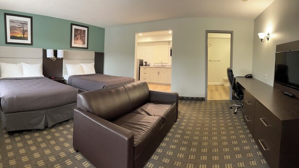 Quarto de hotel com duas camas, um sofá, uma TV e uma kitchenette.