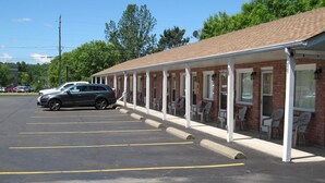 Um motel com área de estacionamento coberta e uma fileira de quartos térreos, cada um com janela individual e espaço para sentar ao ar livre.