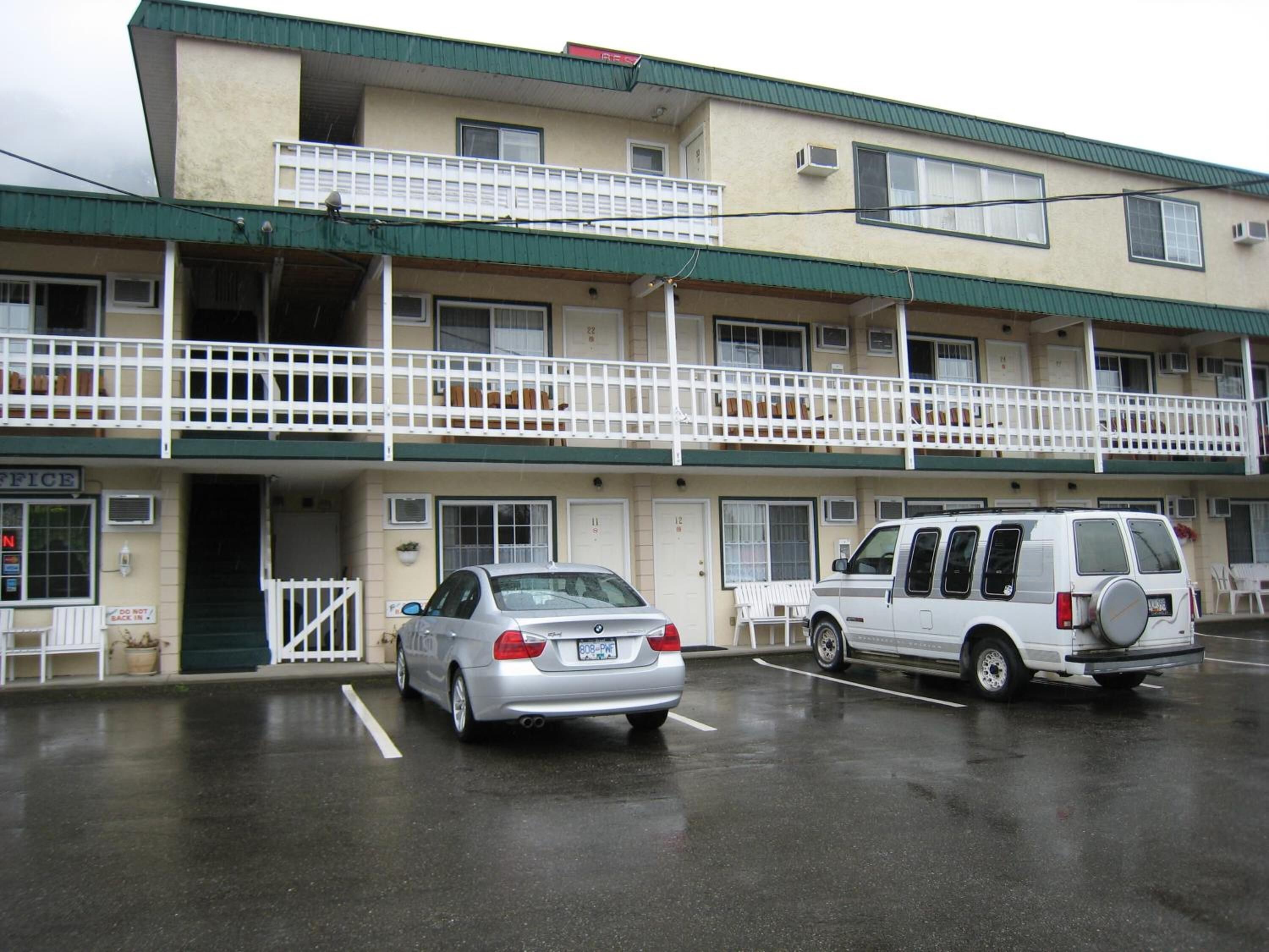 Um motel de vários andares com telhado verde, um carro estacionado em frente e uma van branca.