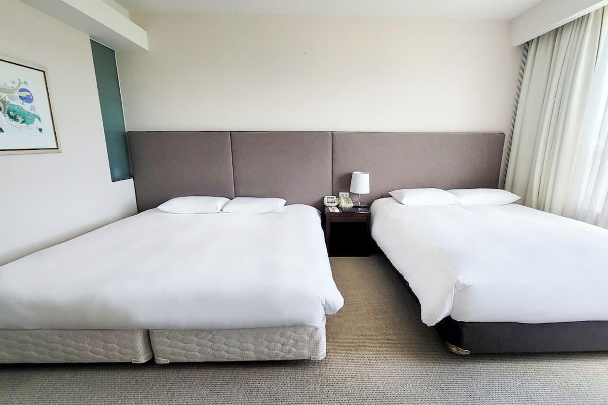 Quarto de hotel com duas camas, uma mesinha de cabeceira, um abajur e um quadro na parede.