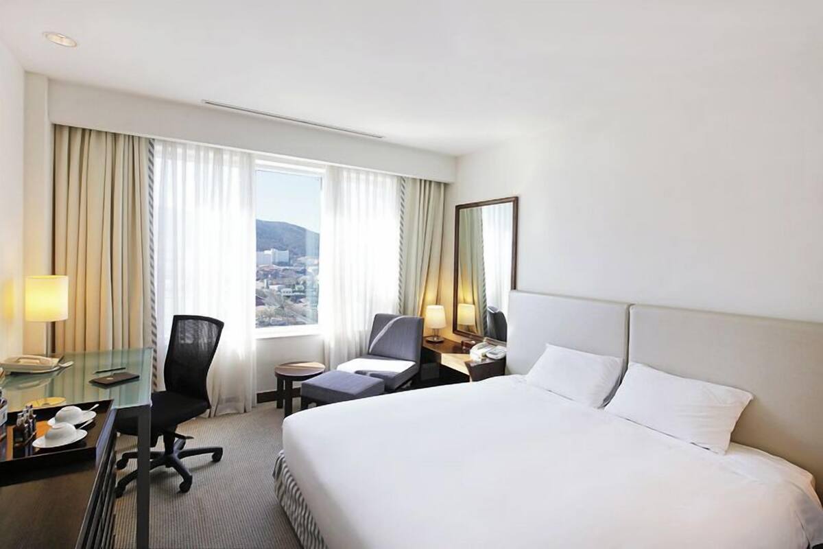 Quarto de hotel com cama grande, escrivaninha, cadeira, mesa pequena e vista para a cidade.