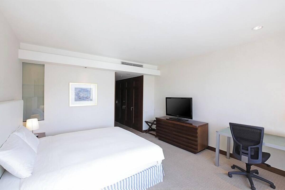 Quarto de hotel com uma cama, televisão, escrivaninha e cadeira.