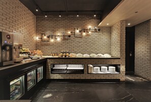Cozinha moderna com parede de tijolos, máquina de café e um balcão de buffet com diversos alimentos e utensílios.