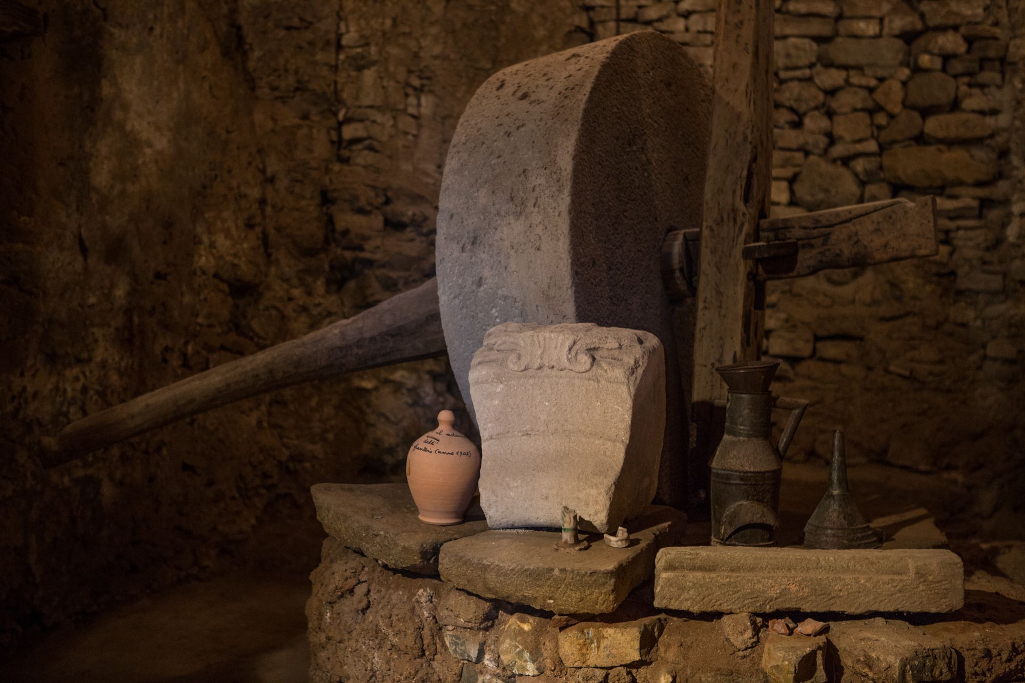 Uma estrutura de pedra com uma grande roda de pedra, um pequeno pote de barro e objetos de metal.