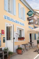 Um hotel com mesas ao ar livre e uma placa indicando 'Le Relais des Deux Vallées'.