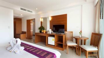 Quarto de hotel com cama, escrivaninha, televisão, mini-geladeira e duas cadeiras.