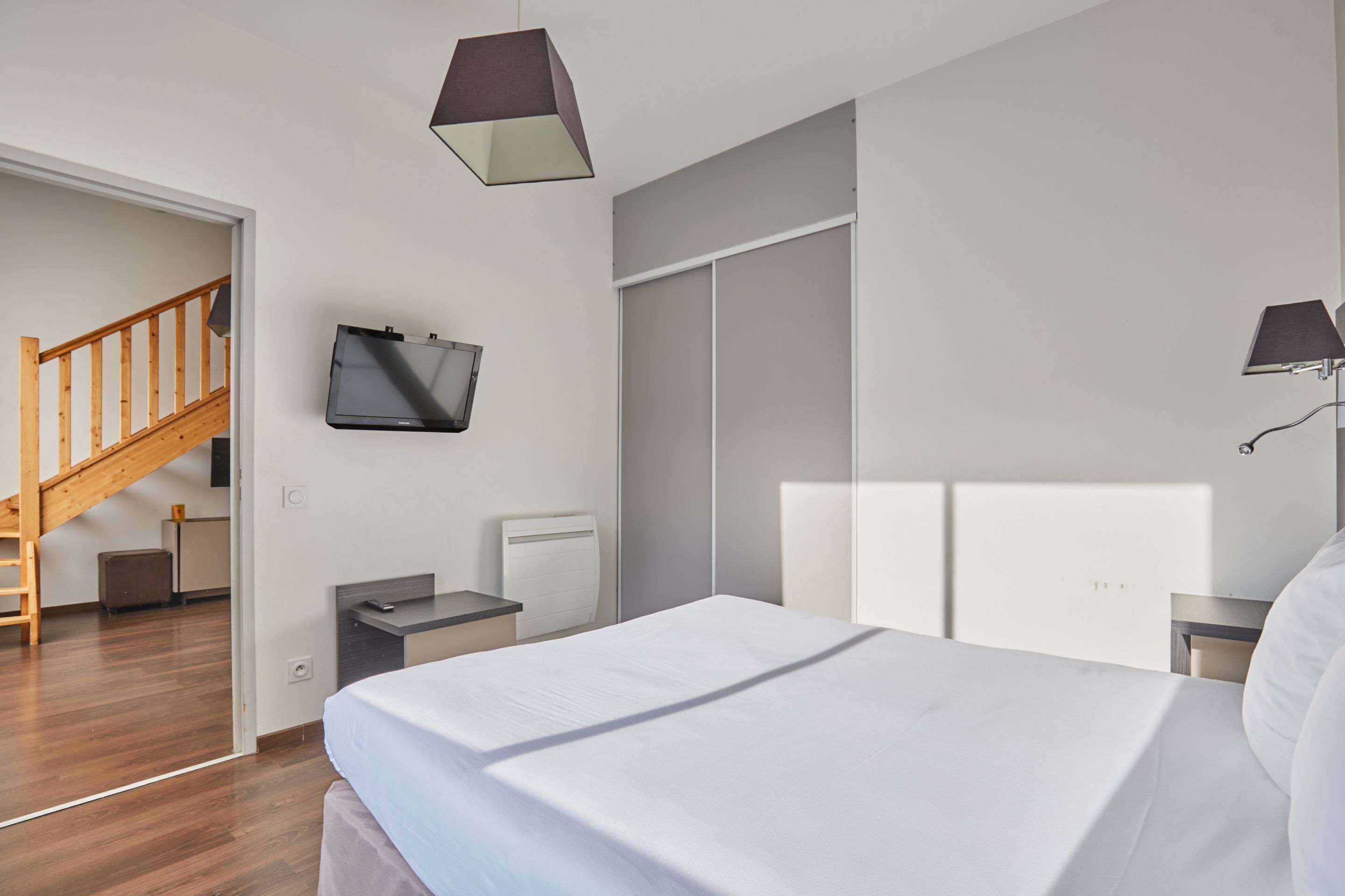 Quarto com cama, televisão na parede, guarda-roupa e escada para outro cômodo.
