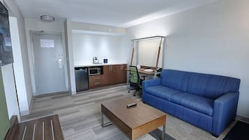 Quarto de hotel compacto com cozinha compacta, um sofá azul, uma mesa de centro de madeira e um tapete pequeno.