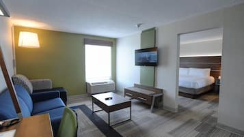Quarto de hotel com sofá, escrivaninha, televisão, cama e janela.
