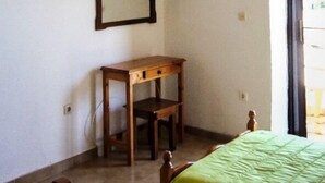 Quarto com uma cama, uma escrivaninha de madeira, uma televisão e uma luminária no teto.