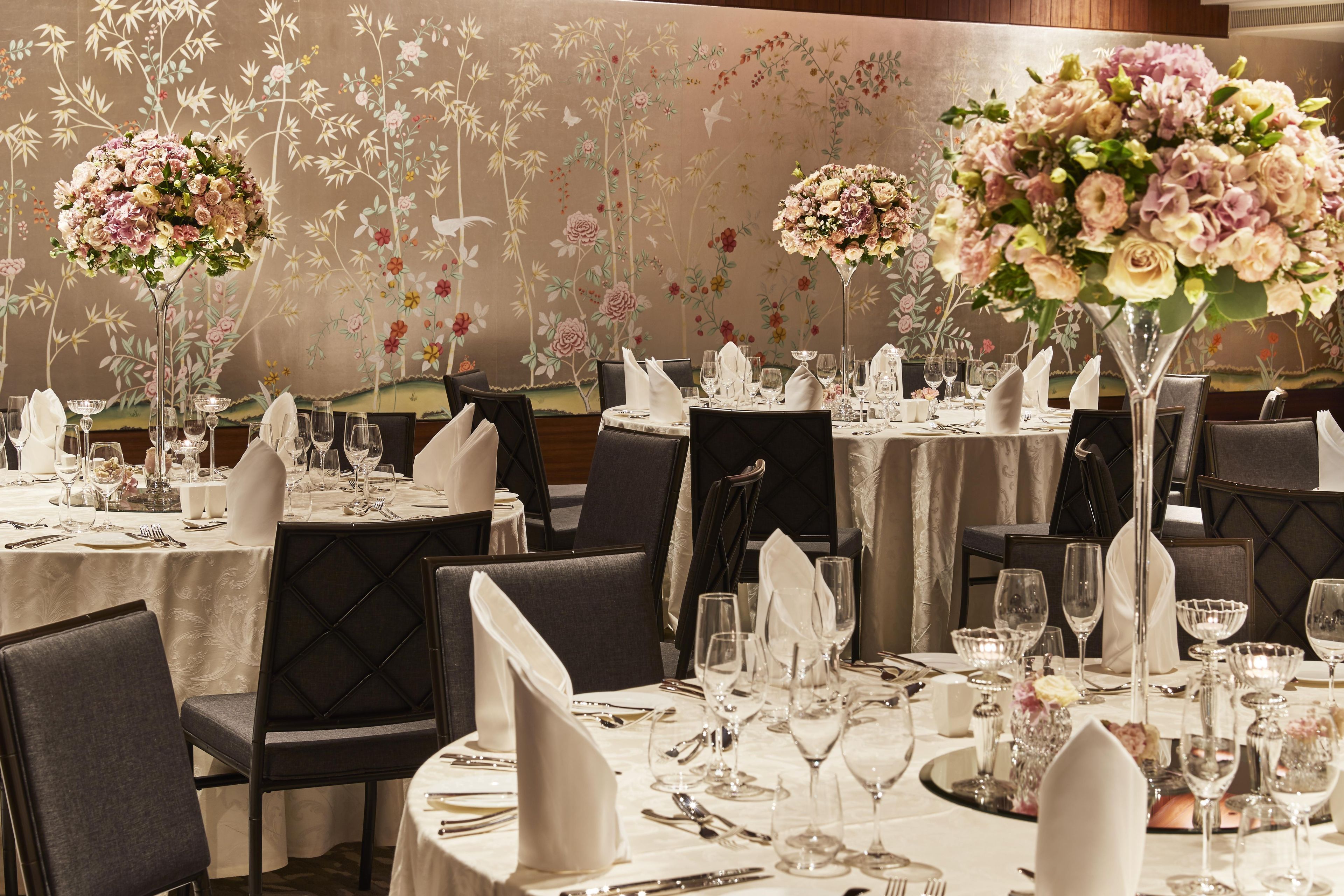Um ambiente de jantar formal com várias mesas, cada uma com toalhas brancas, talheres e copos de vidro.