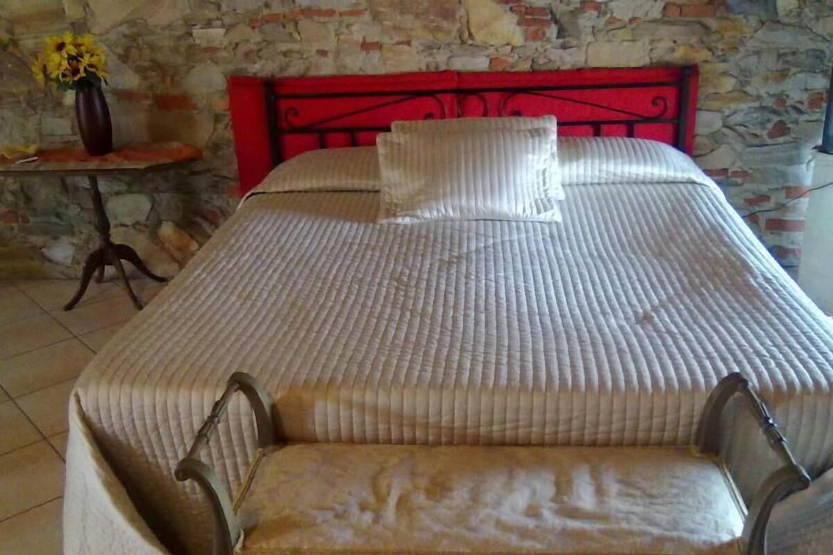 Uma cama com colcha listrada e almofadas, uma pequena mesa de cabeceira com um vaso de flores e uma cadeira com um encosto macio.