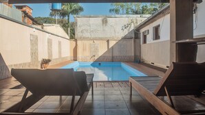 Uma área de piscina com duas espreguiçadeiras, piso de azulejos e parede de concreto.