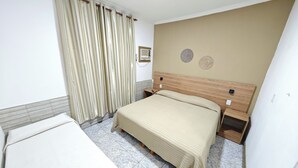 Quarto de hotel com cama, mesa de cabeceira e um pequeno criado-mudo de madeira.