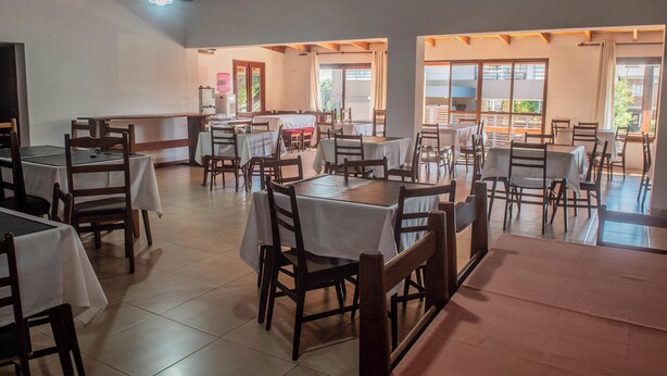 Uma sala de jantar espaçosa com várias mesas e cadeiras, janelas amplas e teto de madeira.